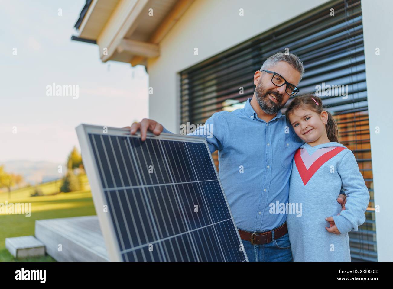 Father with his little daughter near their house with solar panels ...