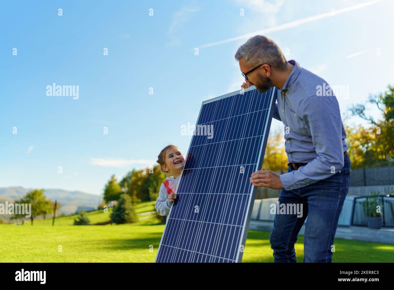 Father with his little daughter catching sun at solar panel,charging at ...