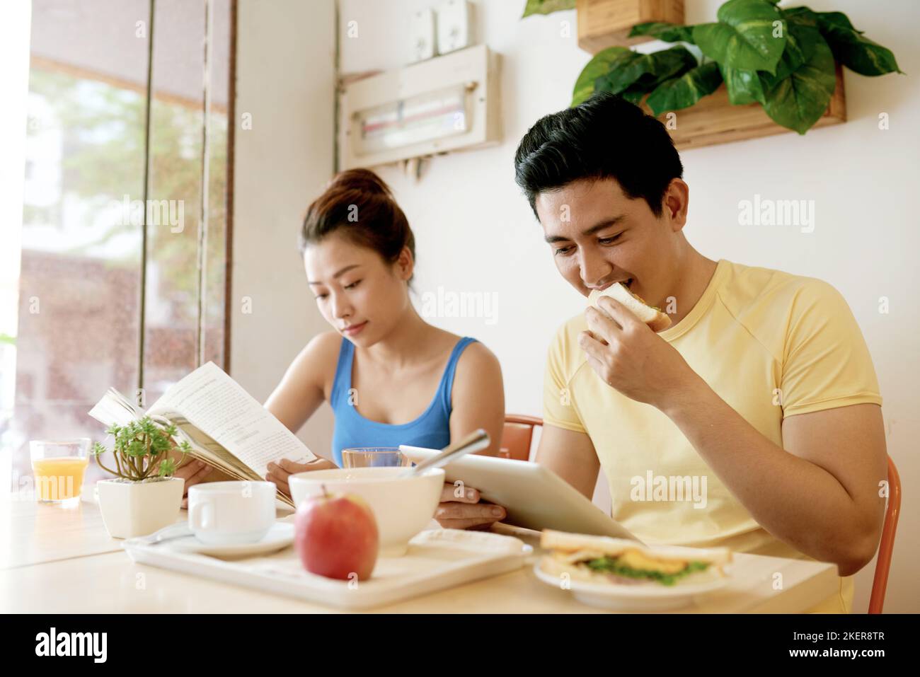 Young Vietnamese couple eating breakfast and reading books at home ...