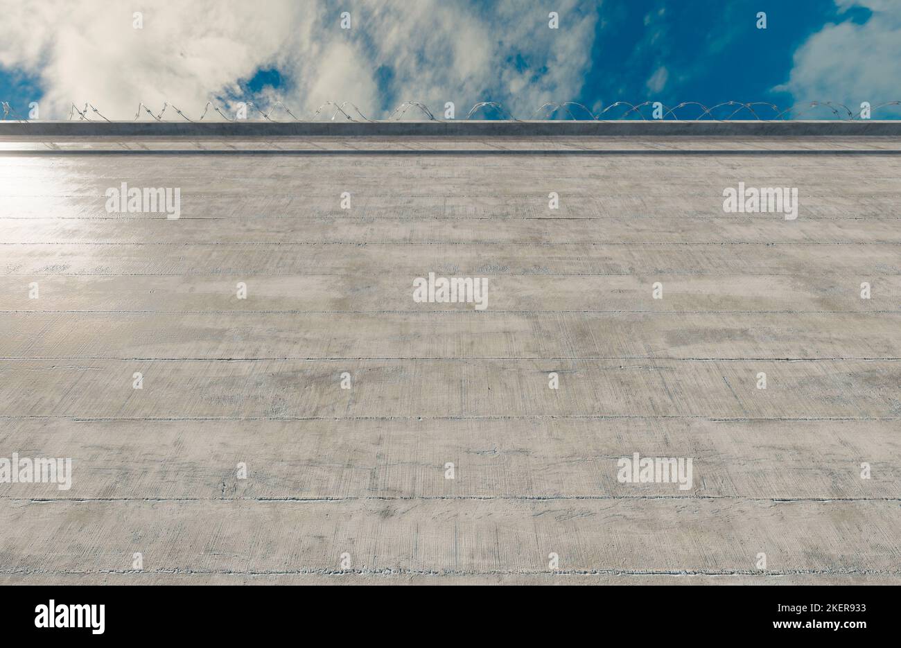 A massively high concrete security boundary wall topped with barbed ...