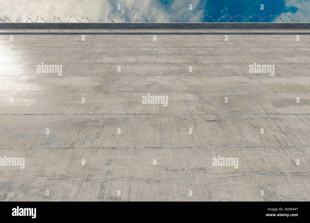 A massively high concrete security boundary wall topped with barbed ...