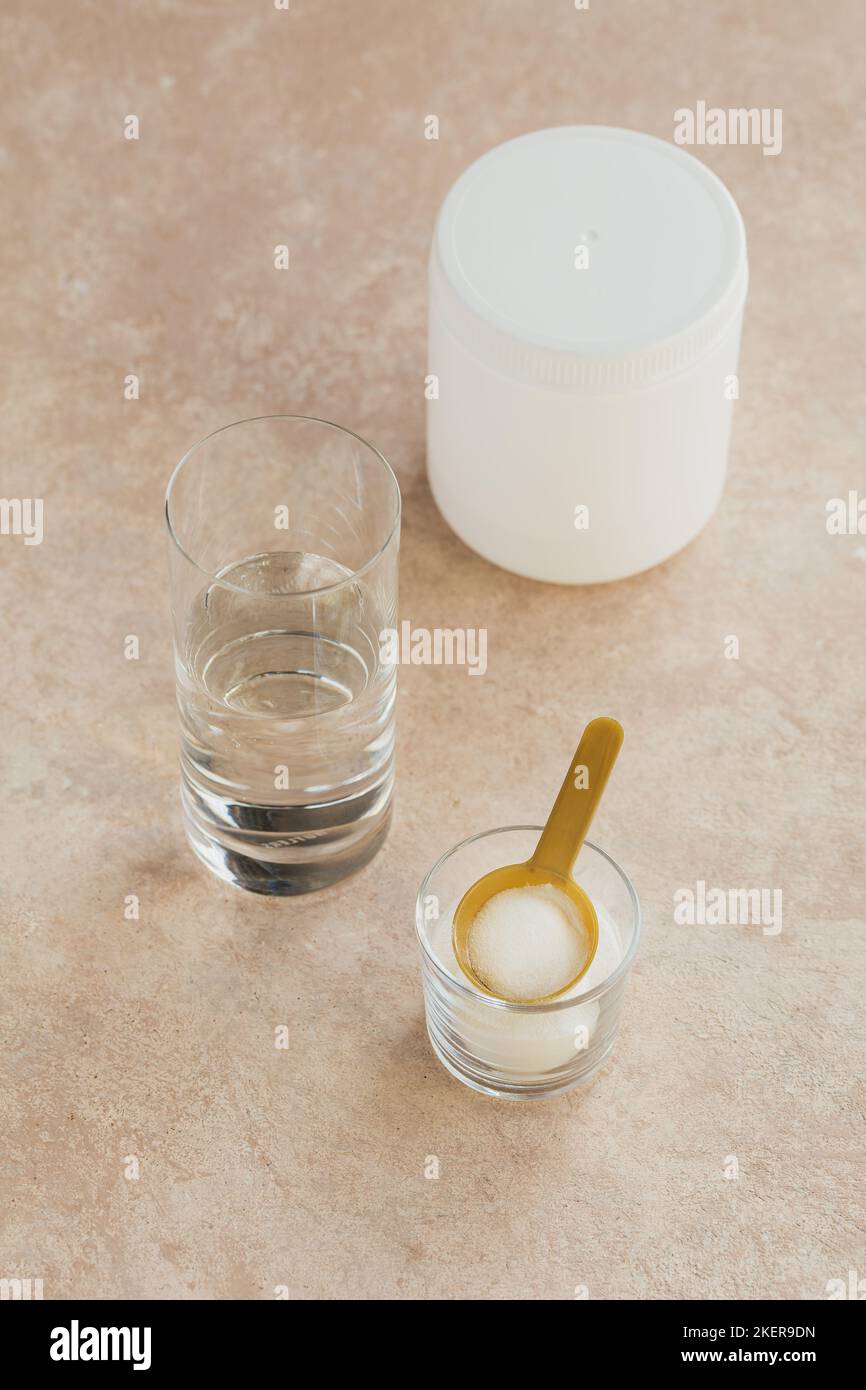 Collagen powder in bowl, glass of water and measure spoon on a light ...