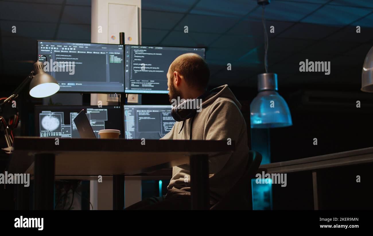 System Programmer Typing Source Code On Laptop And Multiple Monitors Using Programming Language