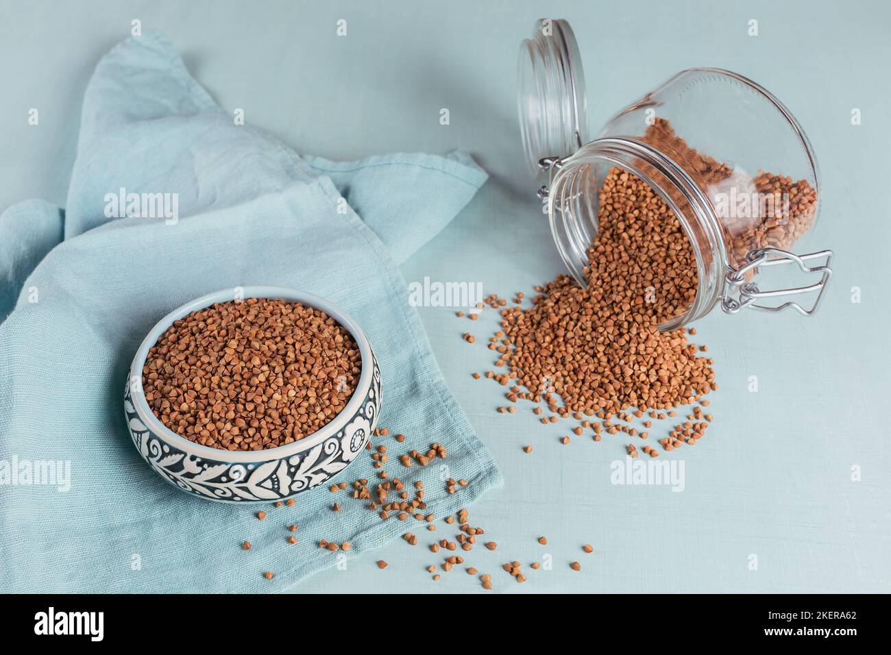Bowl of dry raw buckwheat groats and glass jar on a light blue ...