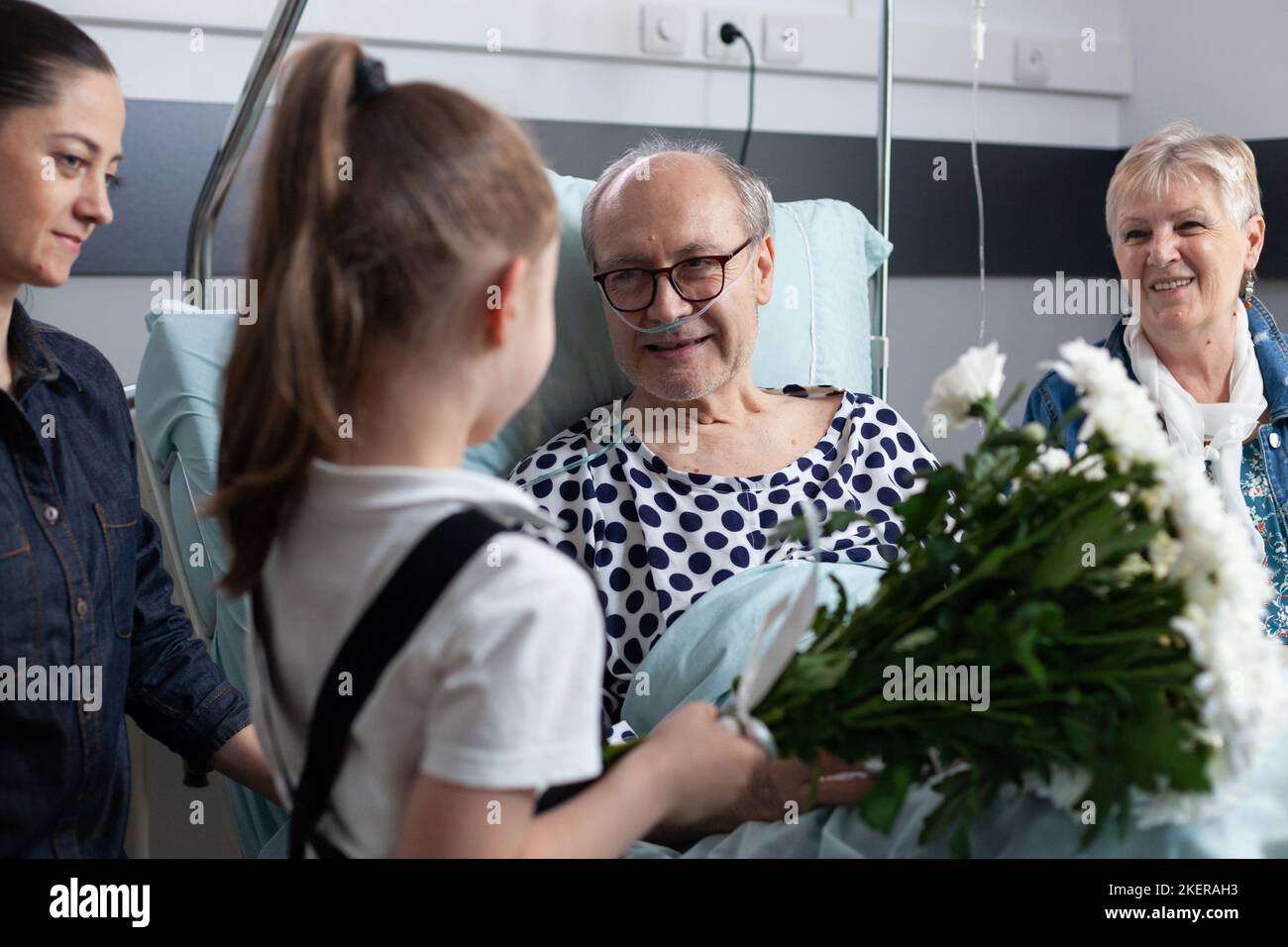 Sick grandfather receiving flowers from granddaughter in hospital room ...