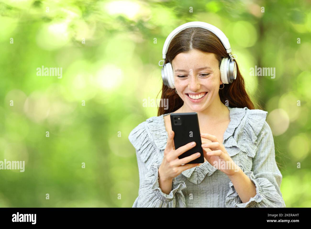 Front view portrait of a happy woman listening to music in a green ...