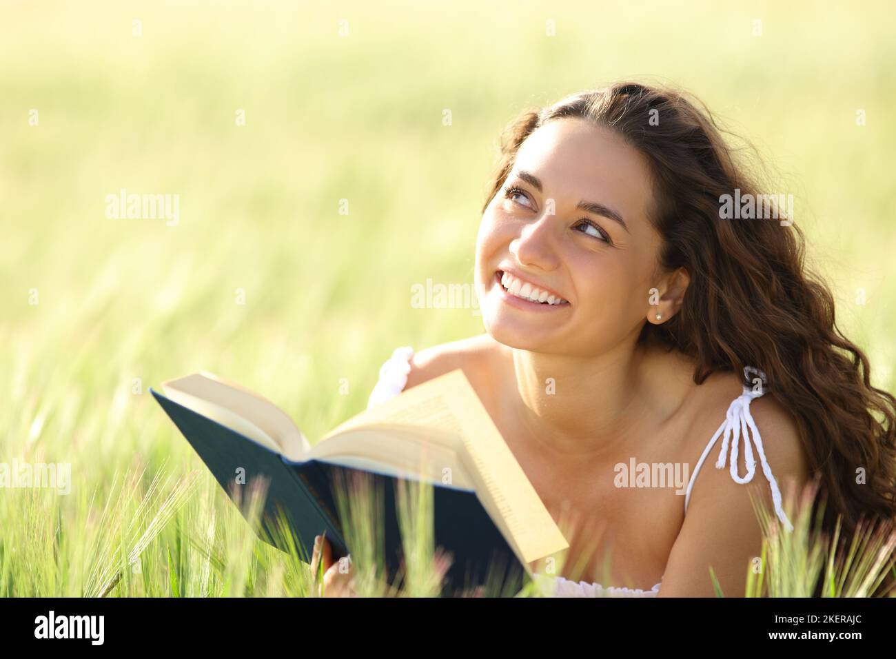 Happy woman reading a book and dreaming looking above in a field Stock ...