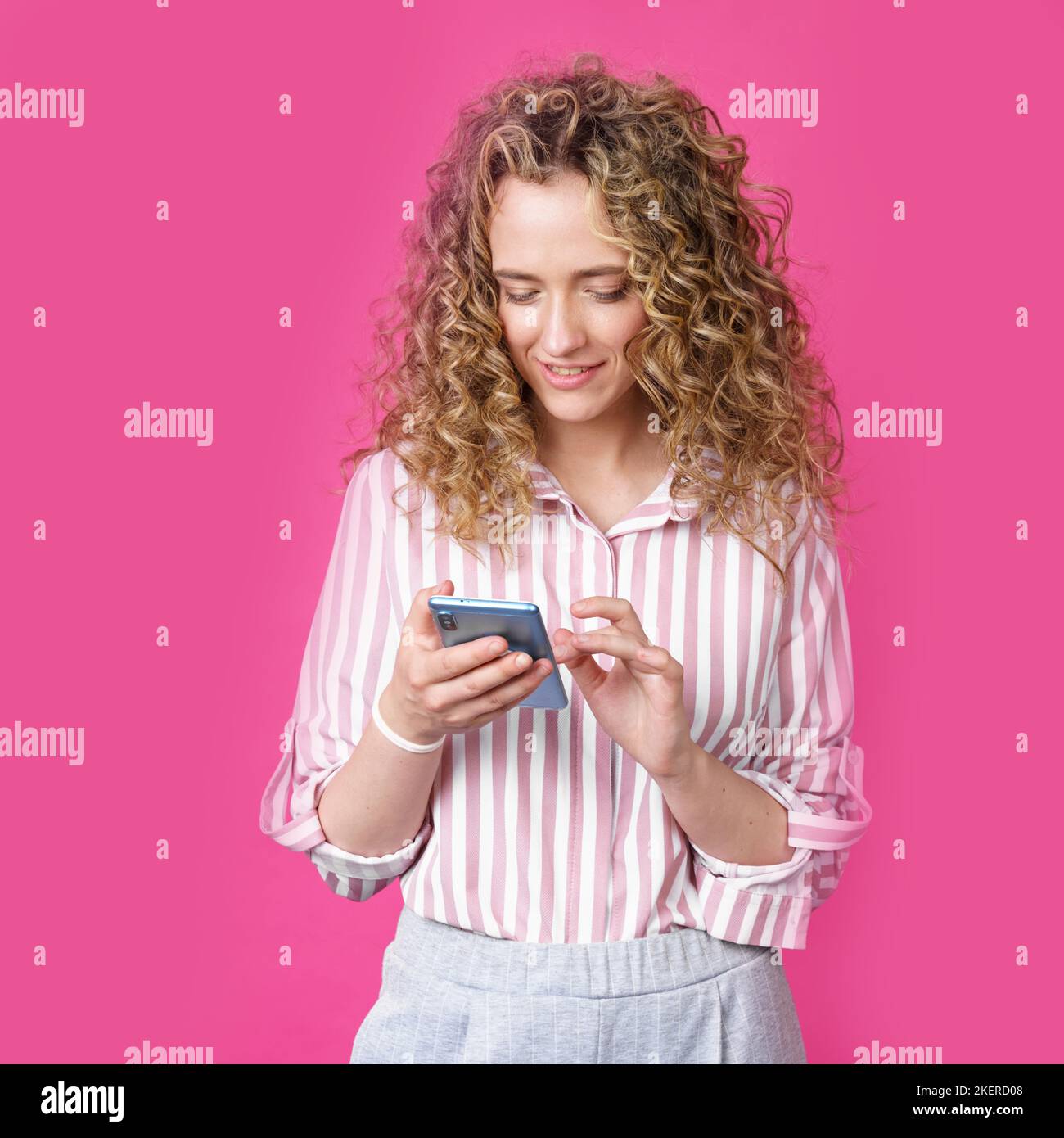 Fashionable woman in a striped shirt, typing a message on the phone and ...