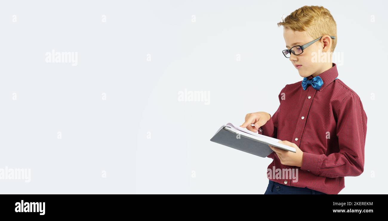 A schoolboy with glasses reads a book he holds in his hands. Isolated ...