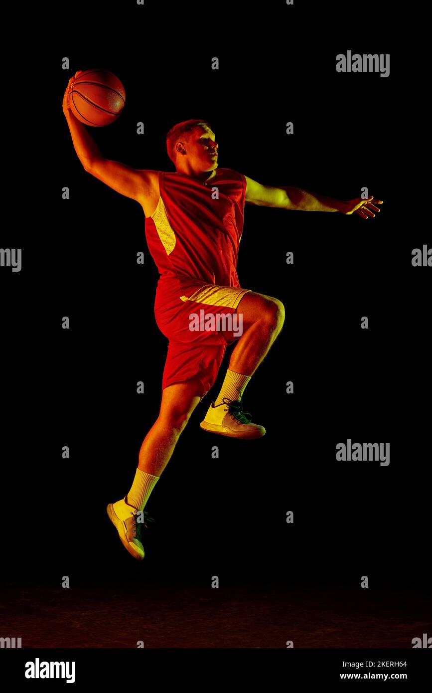 Dynamic portrait of young active athlete, male basketball player in sports uniform practicing ...