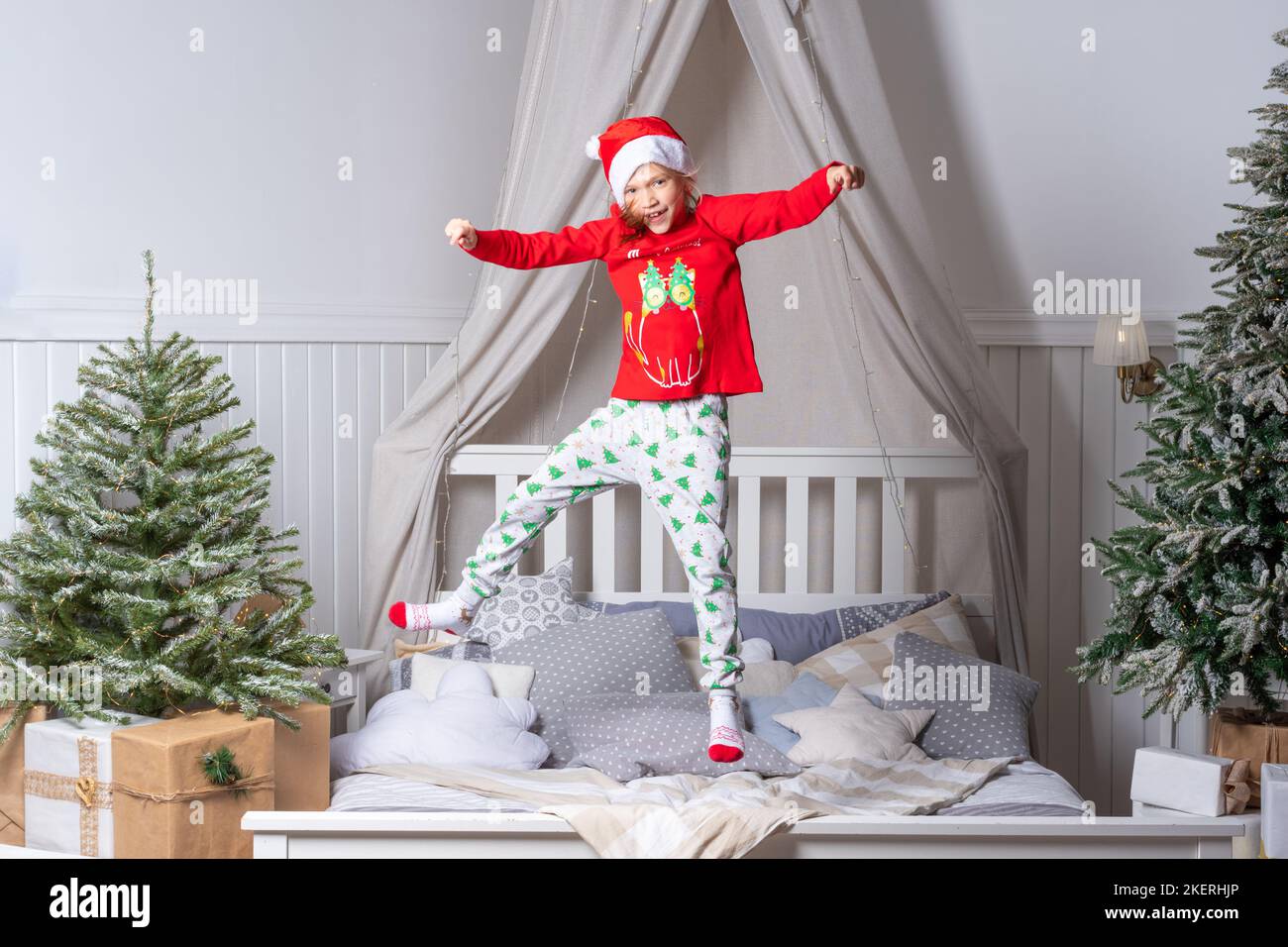 Happy funny baby girl in pajamas and Santa hat jumps in bed on ...