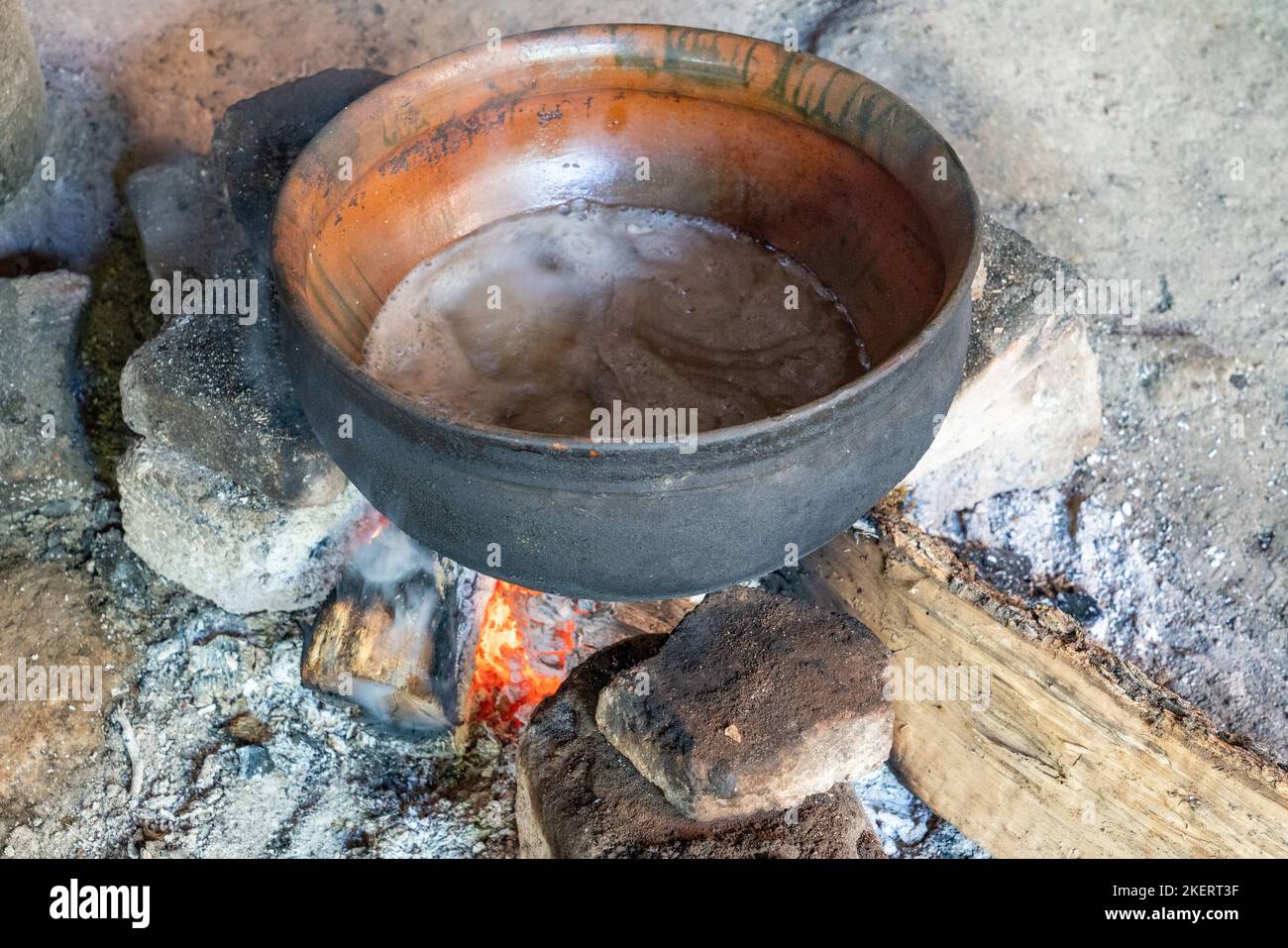 A bowl of beeswax heating over a wood fire to use in making candles in ...