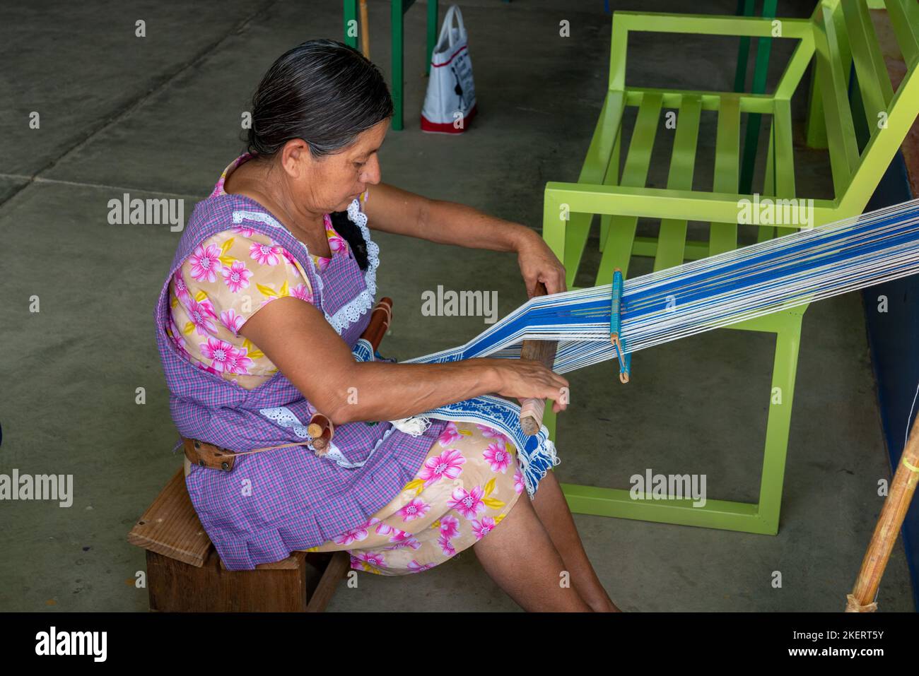 A woman wearing a traditional apron weaves a fabric belt on a ...