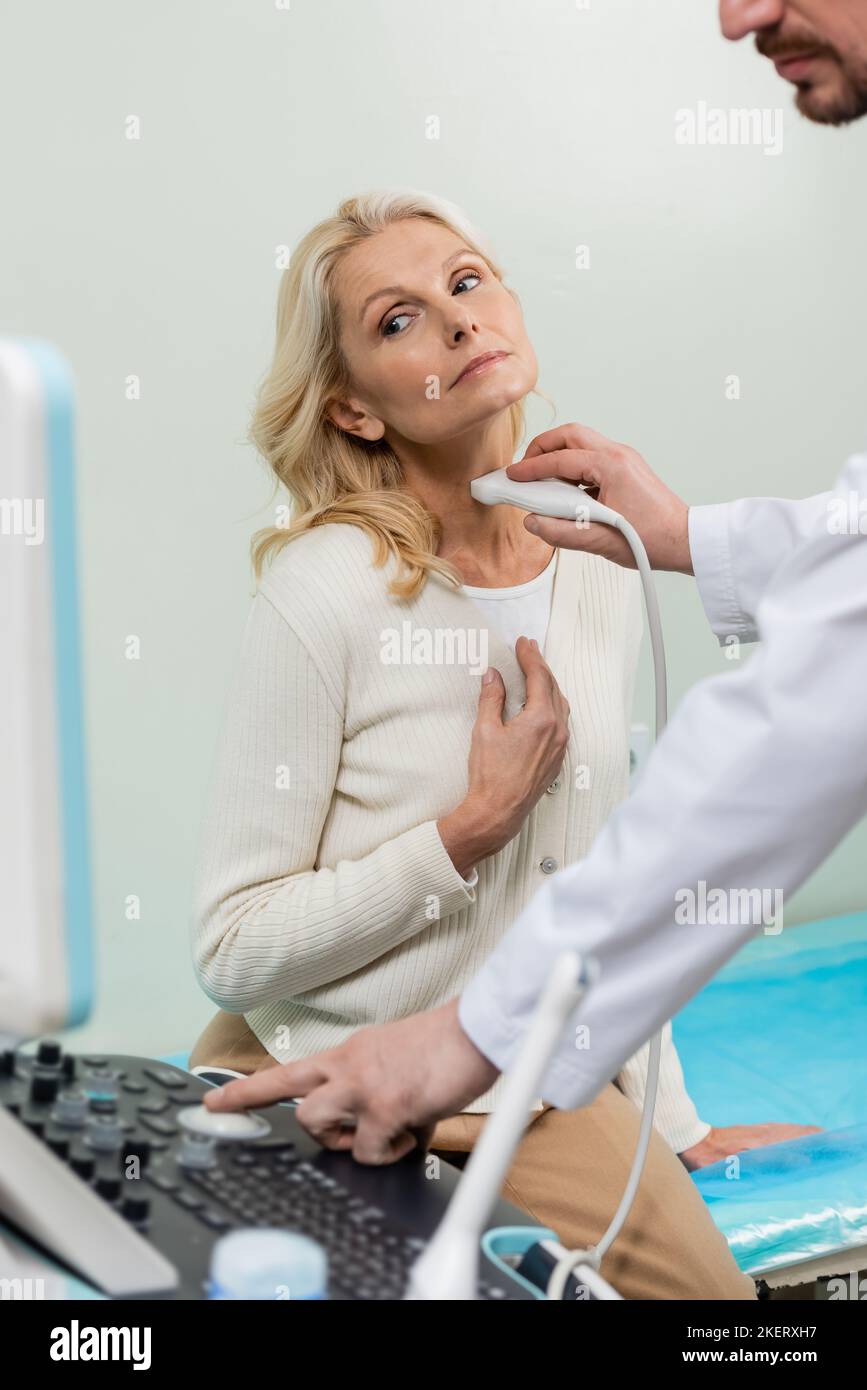 blonde woman looking at ultrasound machine near physician doing diagnostics of her larynx,stock ...