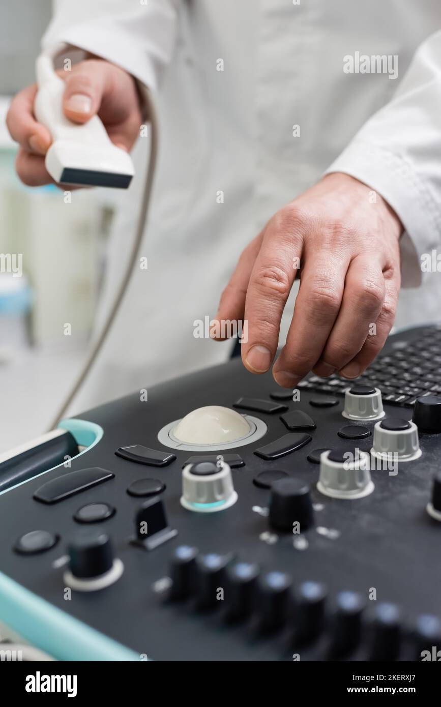 partial view of blurred doctor holding probe while using ultrasound ...