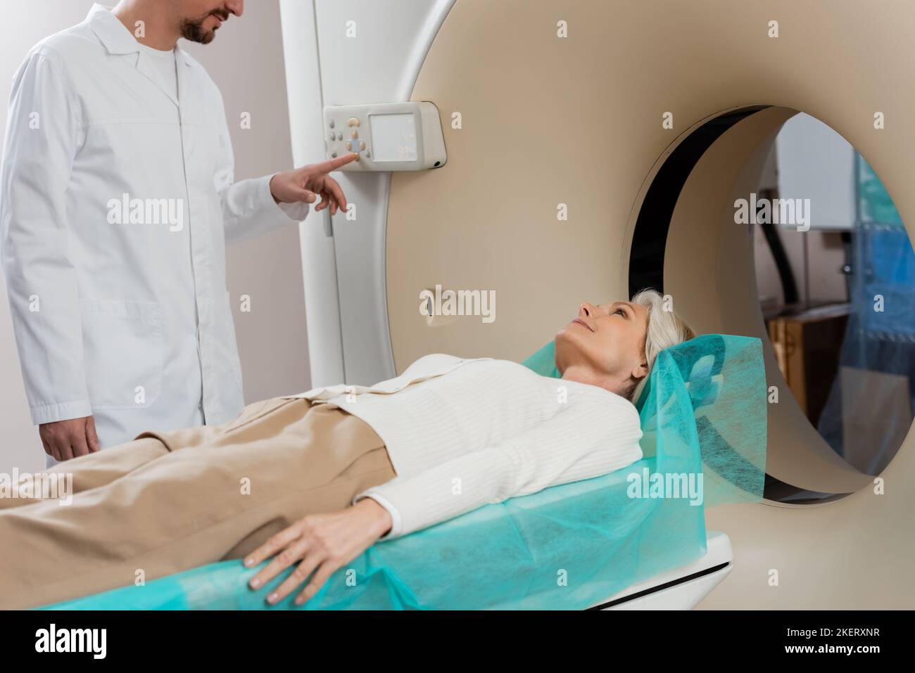 middle aged woman lying near doctor operating ct scanner during ...