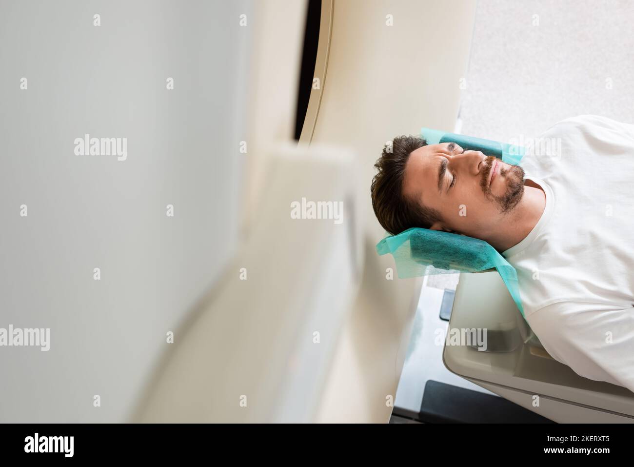 worried man with closed eyes lying during examination on ct scanner in ...