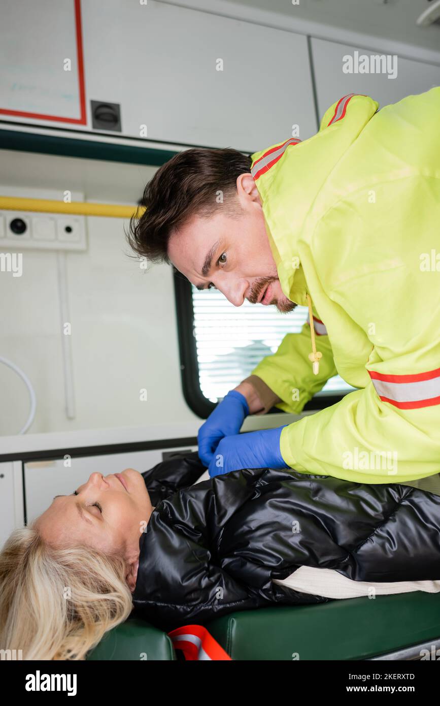 Paramedic in latex gloves giving first aid to unconscious middle aged ...