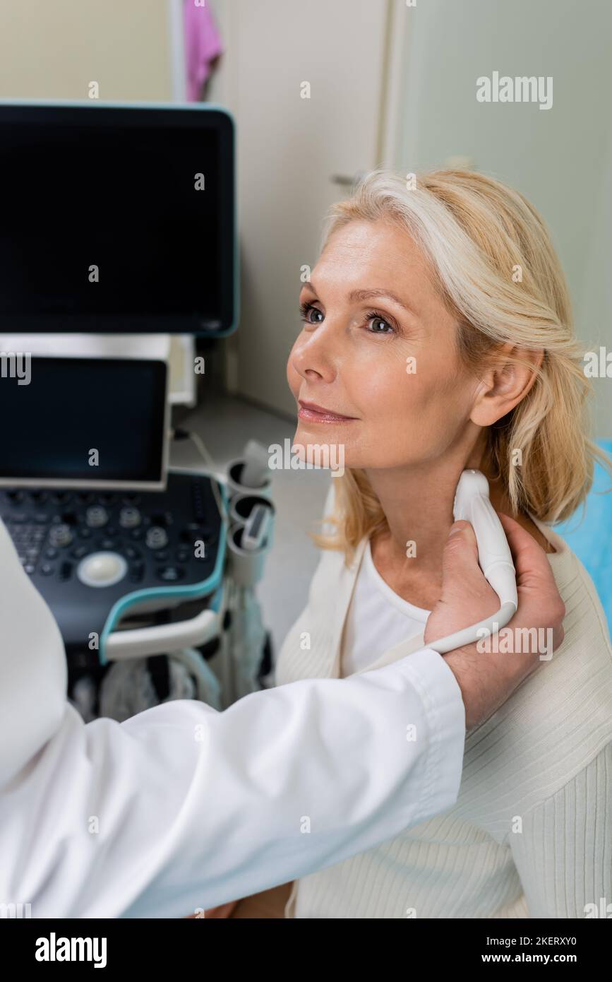 blonde woman smiling near doctor doing ultrasound of her lymph nodes in ...