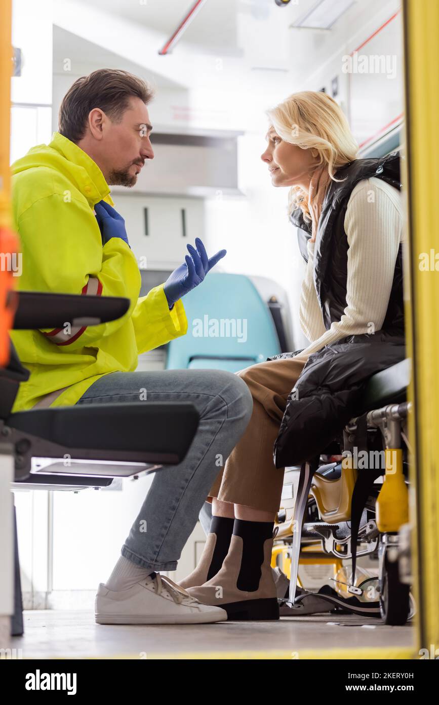 Side view of paramedic gesturing and talking to worried middle aged ...