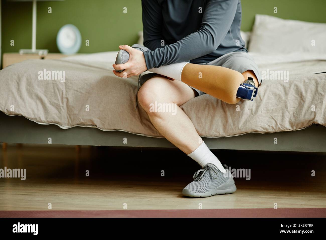 Close up of man setting up prosthetic leg while sitting on bed at home ...