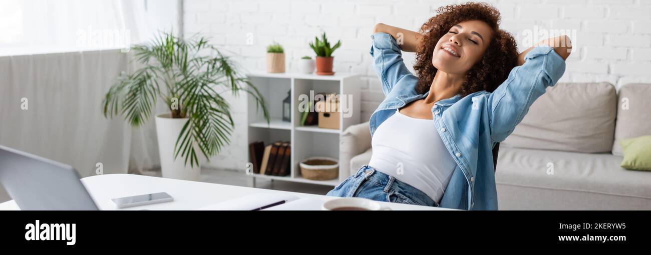 cheerful african american woman with closed eyes resting near workplace ...