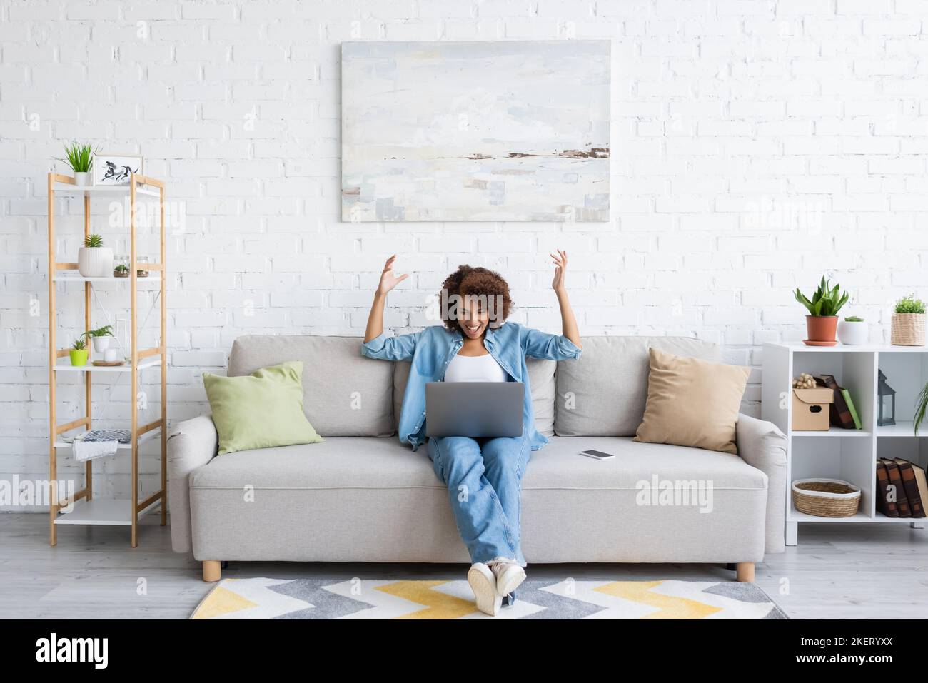 excited african american woman using laptop while sitting on couch and ...