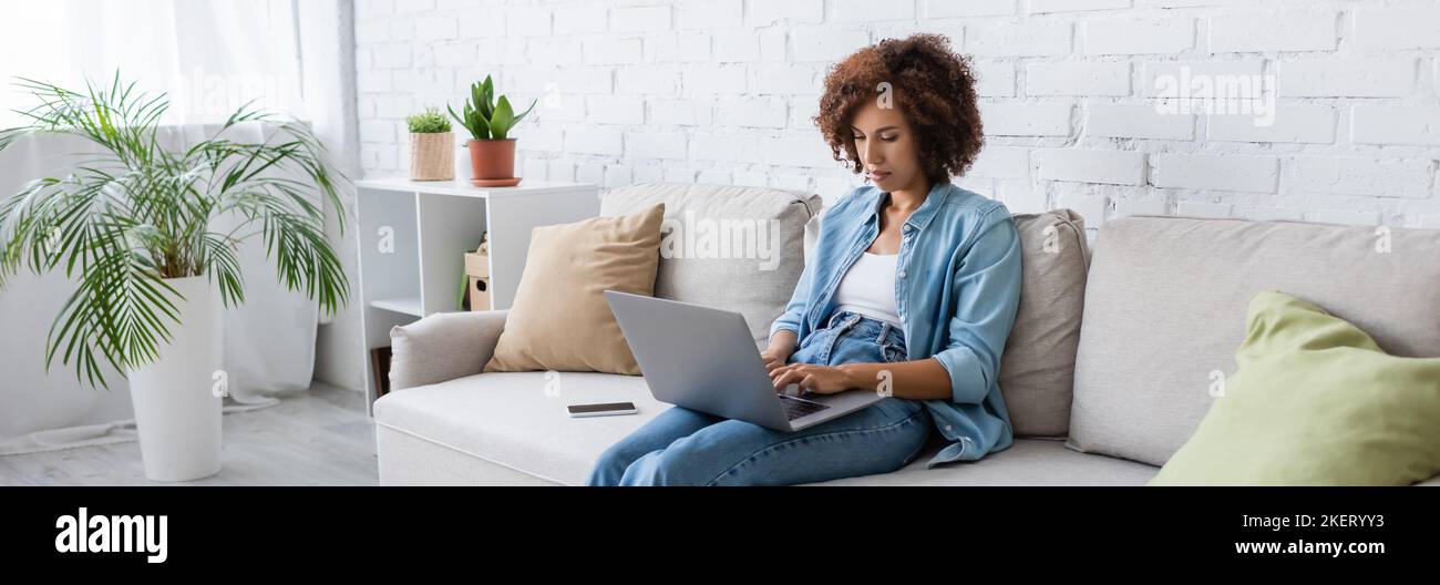 curly african american freelancer using laptop while sitting on couch ...