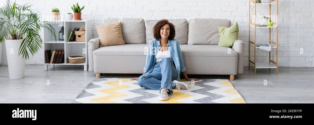 cheerful african american woman sitting on rug with pattern near modern ...