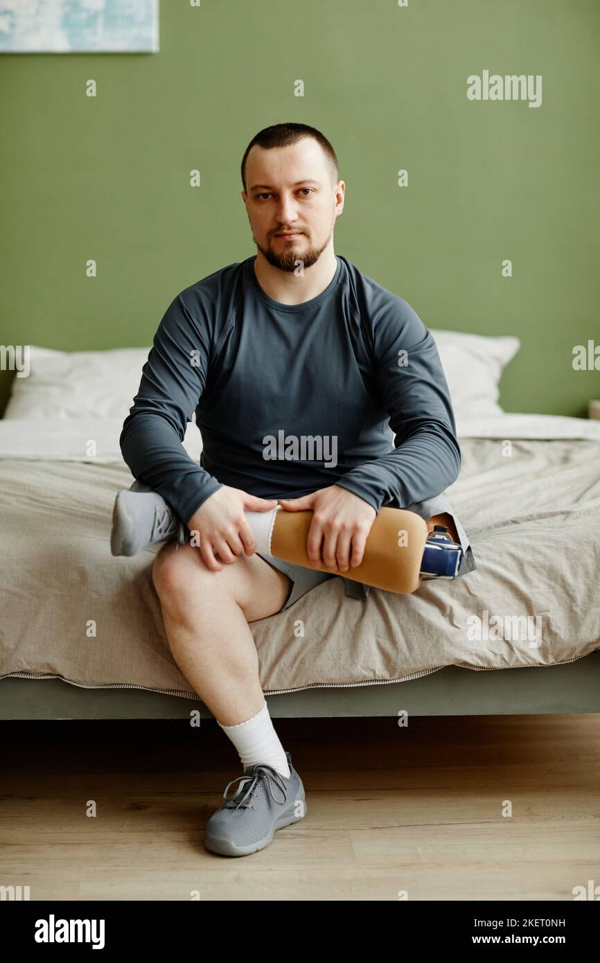 Vertical portrait of man holding prosthetic leg while sitting on bed ...