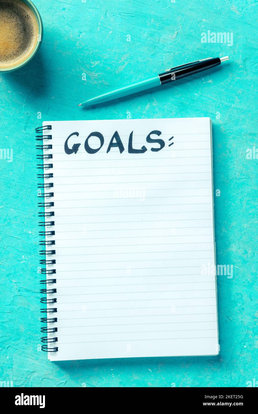 Goals, handwritten word in a notepad with a ballpoint pen and a cup of ...