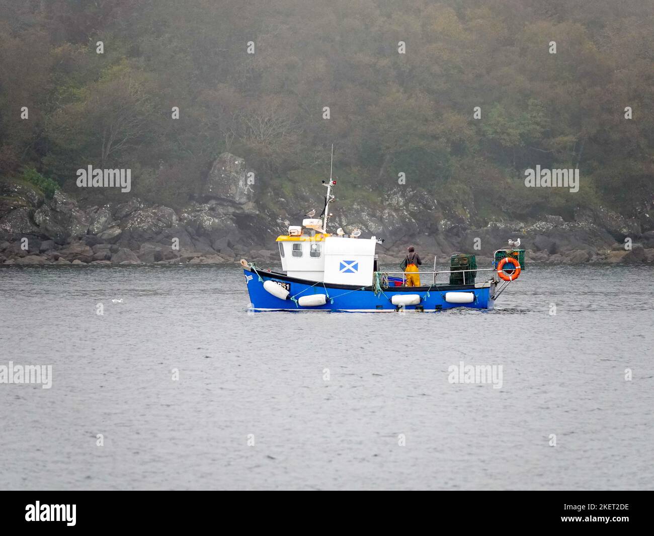 Fisherman tossing out traps from small working boat, in the fog, near ...
