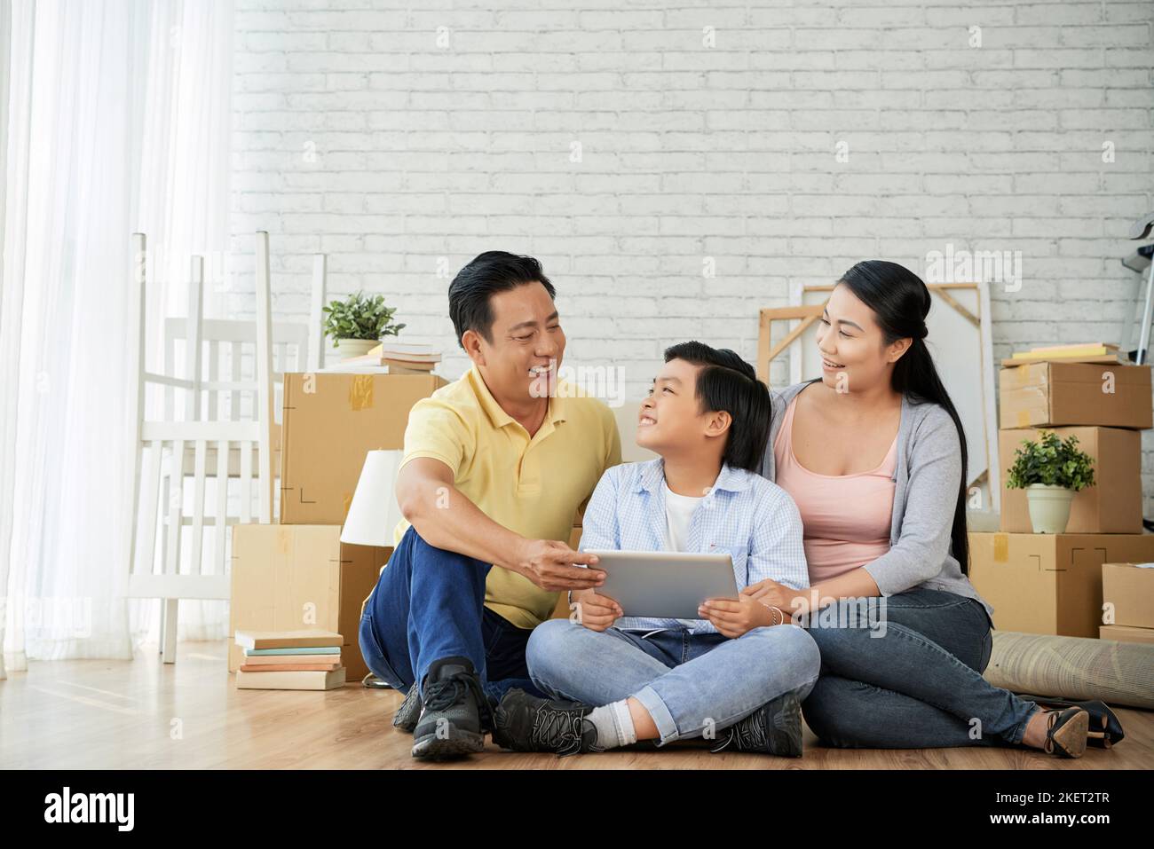 Joyful family of three having fun together while sitting on floor of ...