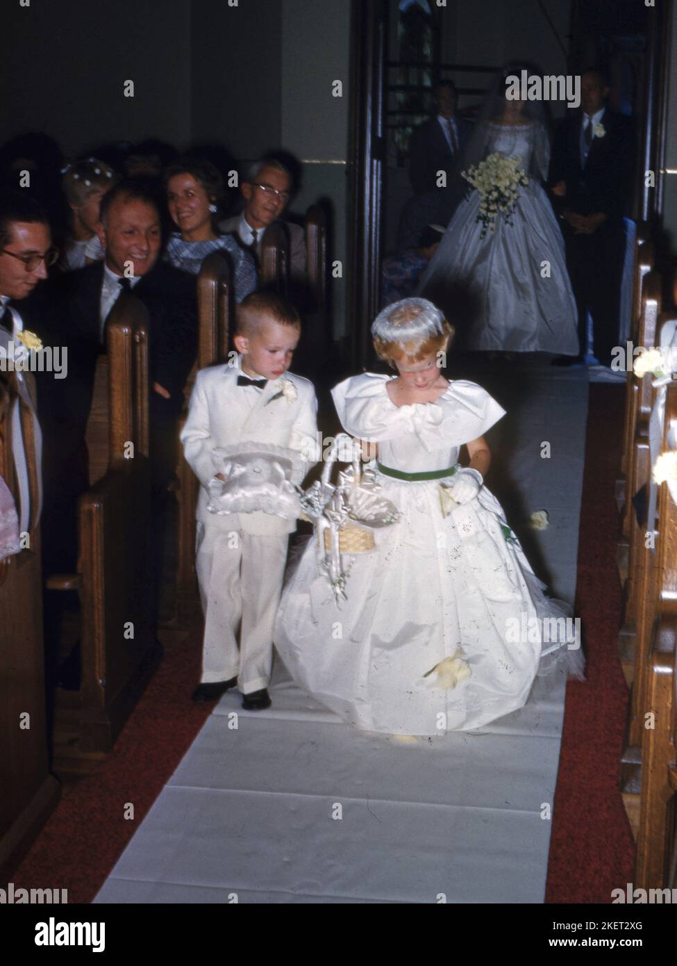 A young page boy and Bridesmaid walking up the aisle as smiling guests ...