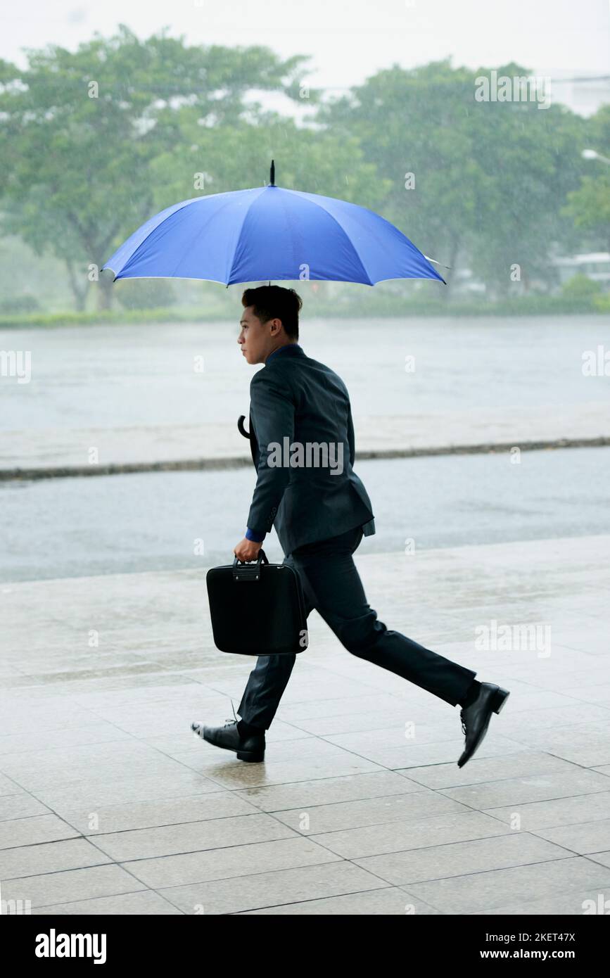 Young Asian manager wearing classical suit holding umbrella in hand and ...