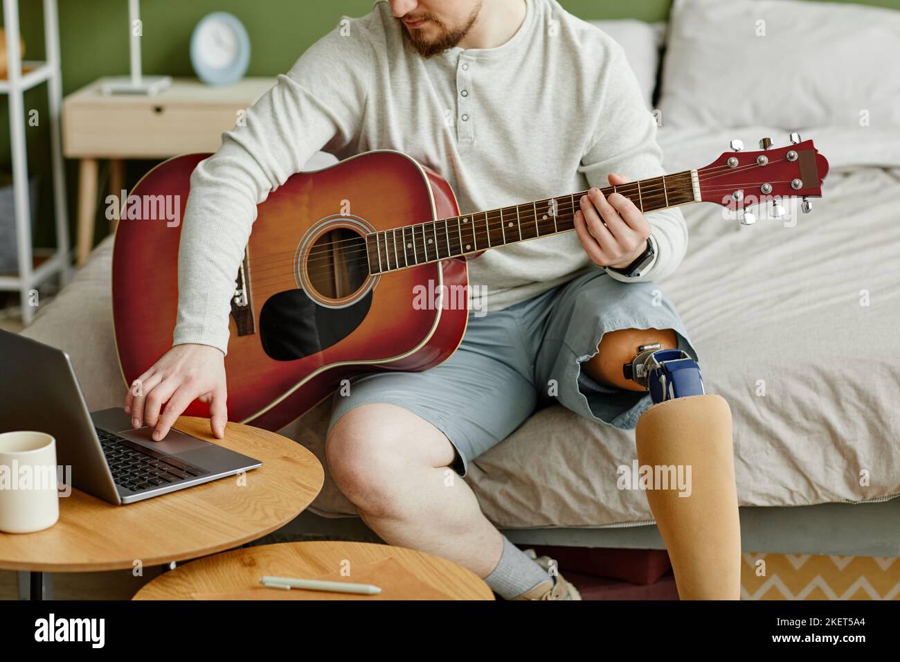 Close up of man with prosthetic leg playing guitar at home and using ...