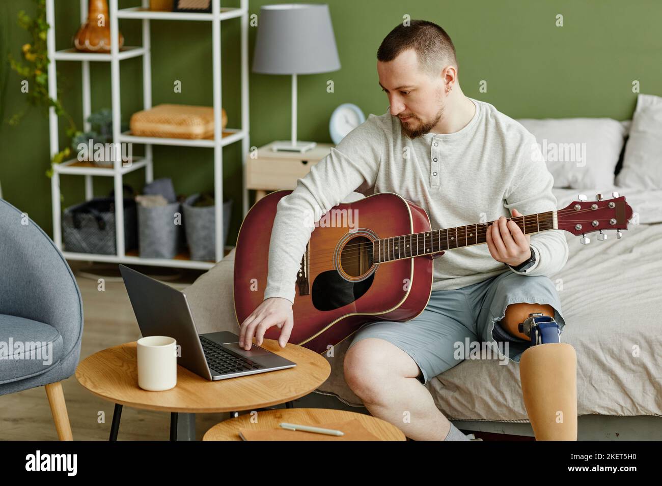 Side view portrait of man with prosthetic leg playing guitar at home ...