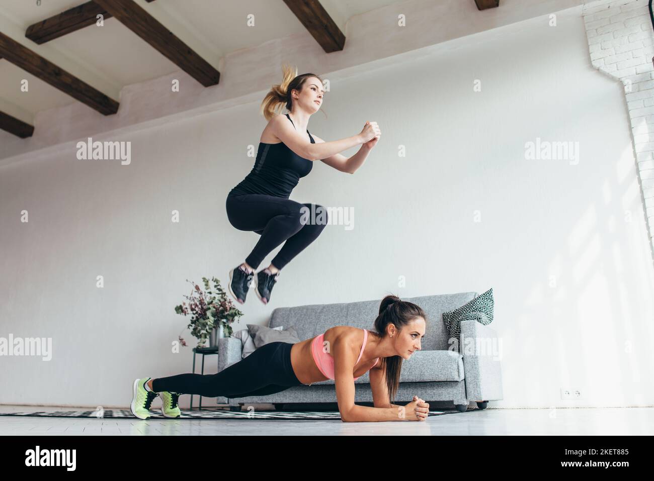 Fit women training home. Girl jumping over her friend while woman ...
