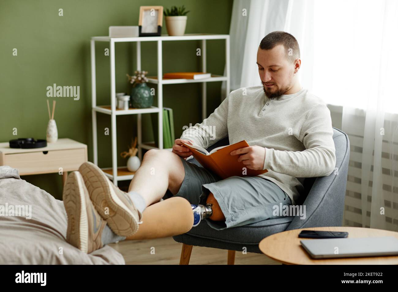 Portrait of adult man with prosthetic leg reading book at home and ...