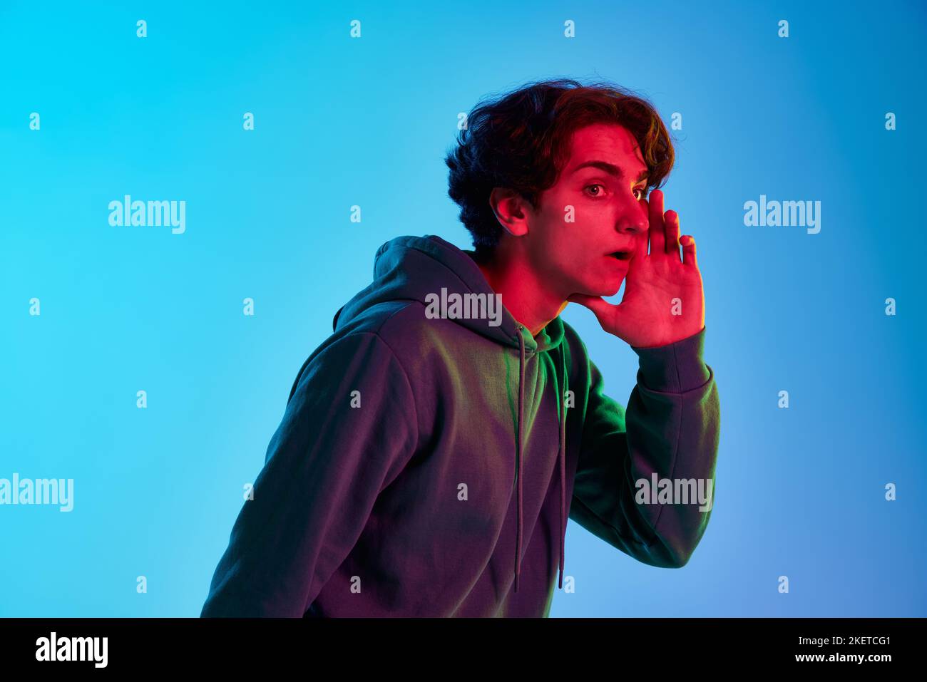 Portrait of young man with curly hair posing with hand to mouth ...