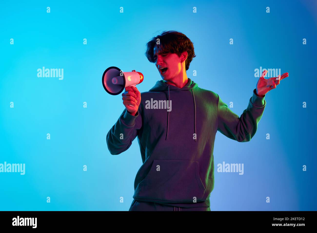 Portrait of young man with curly hair posing, talking on megaphone ...