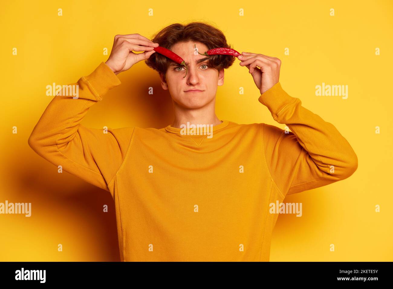 Portrait of young man with curly hair posing with chili pepper isolated ...