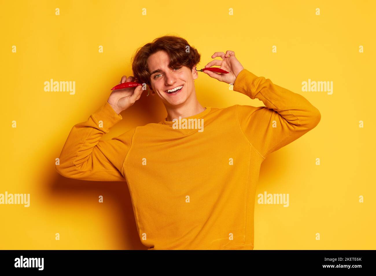 Portrait of young man with curly hair cheerfully posing with chilli ...