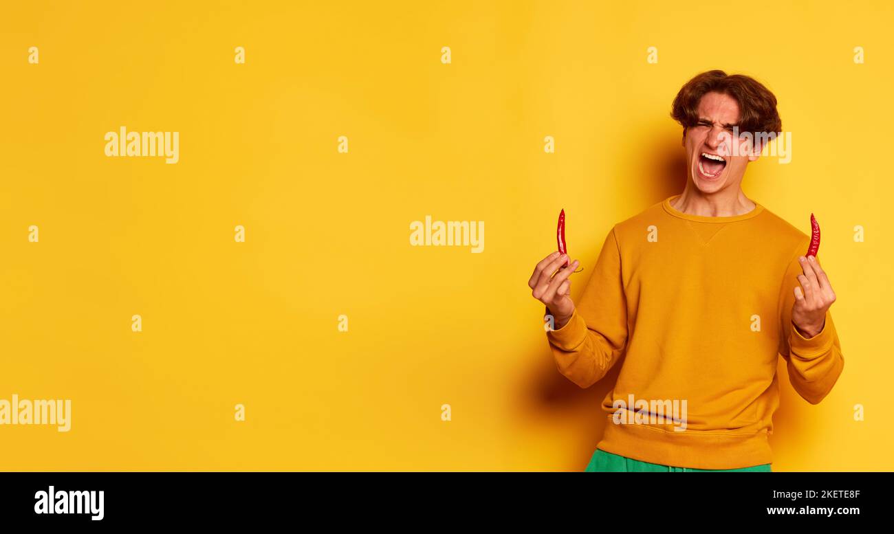 Portrait of young man with curly hair emotively posing with chili ...