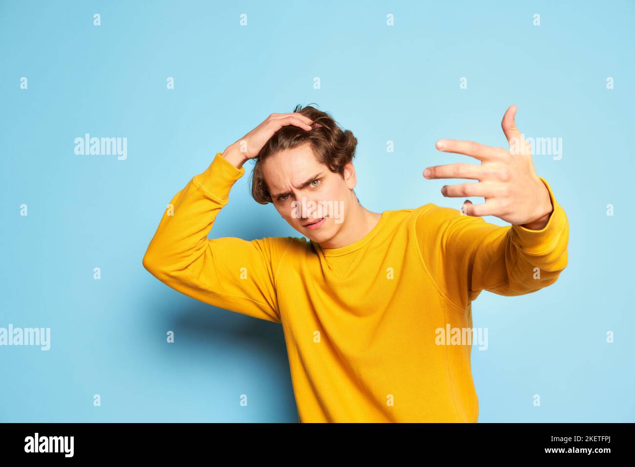 Portrait of young man with curly hair posing isolated over blue ...