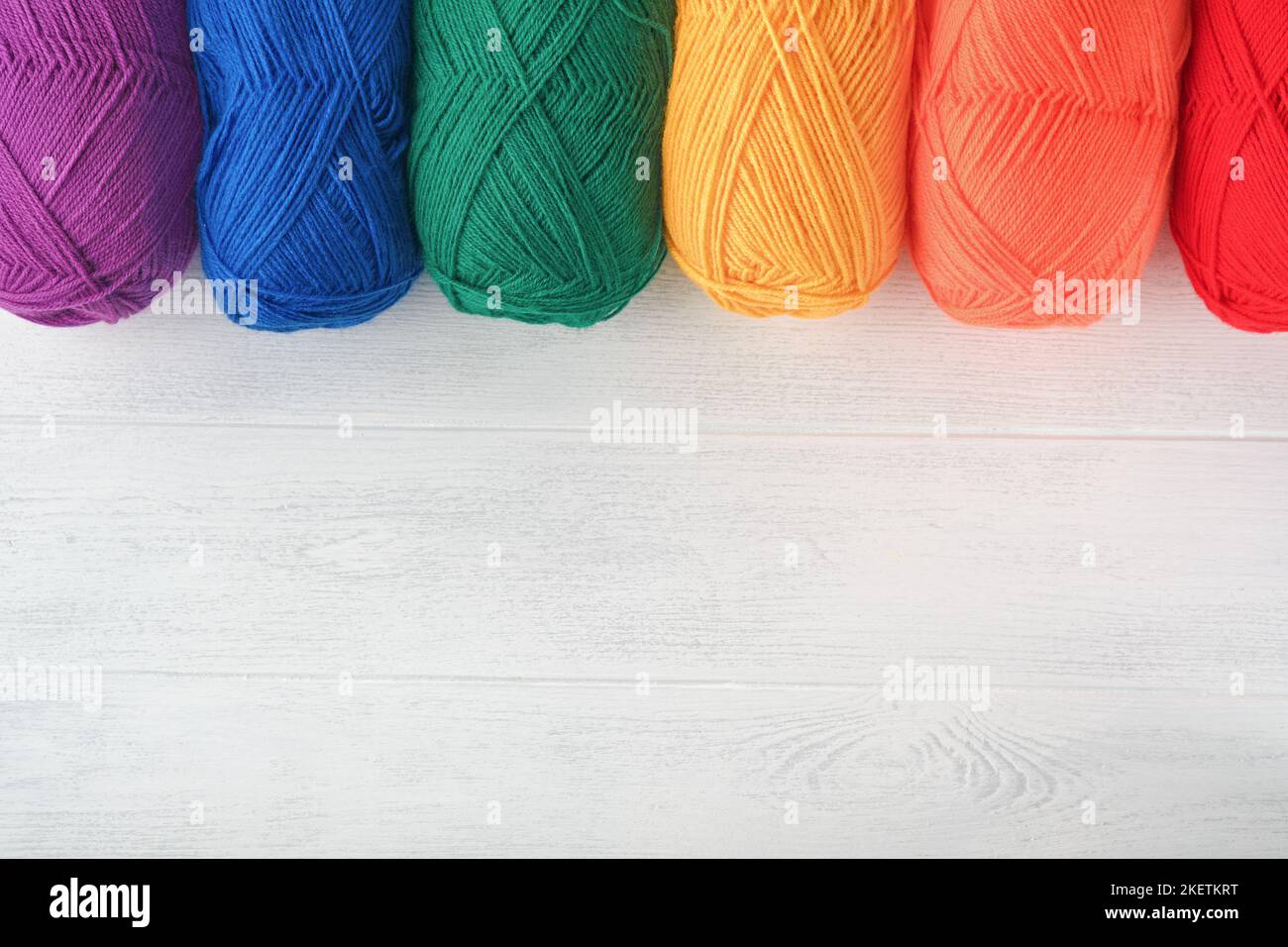 Many multi-colored balls of threads on knitted fabric on white wooden ...