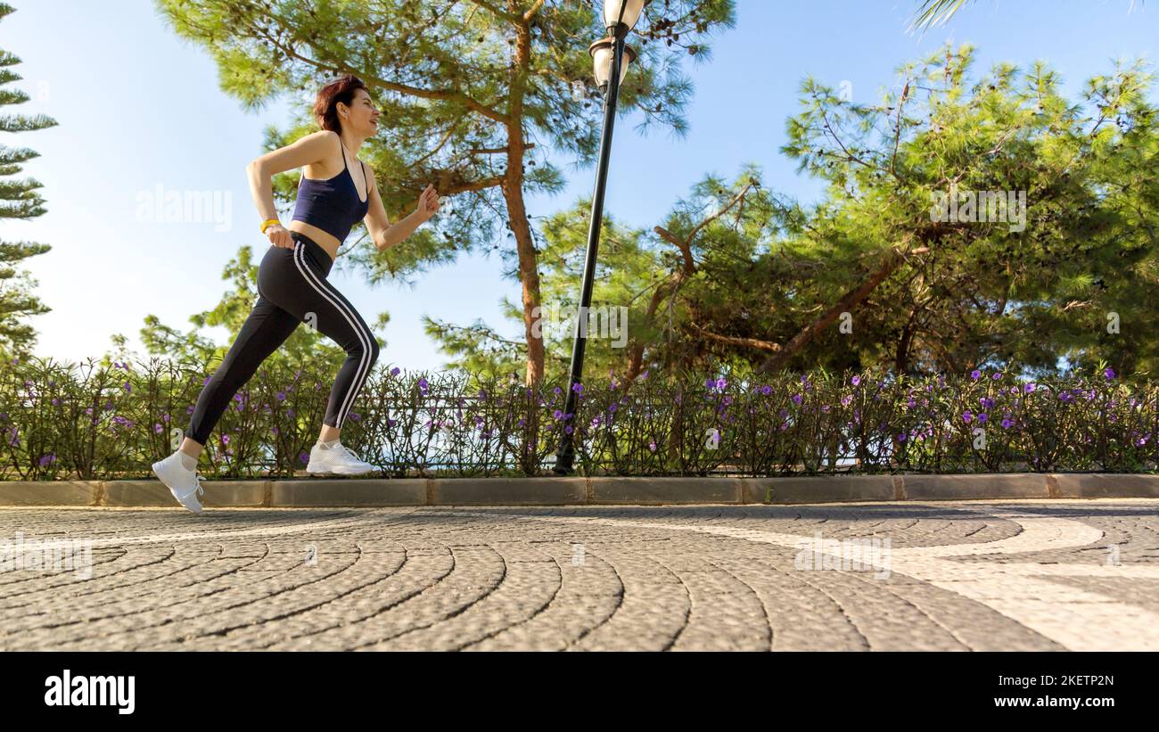 Athlete running along road against background of trees and blue sky ...