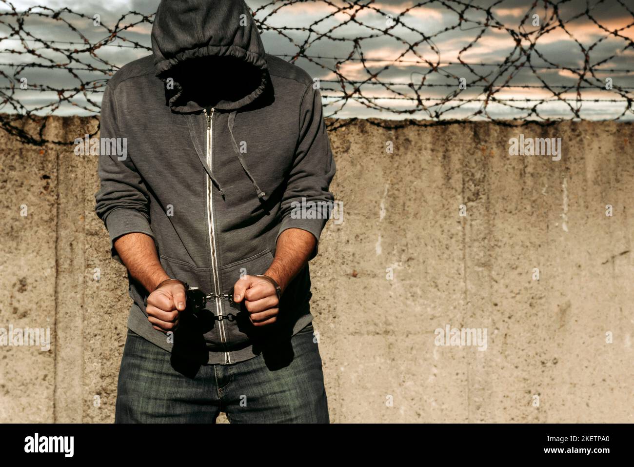 Criminal in jail. A handcuffed man stands against a barbed wire wall ...