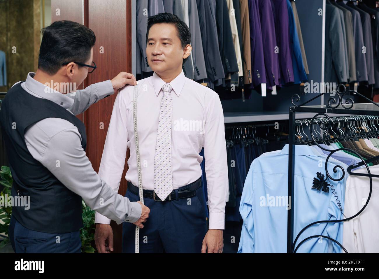 Tailor taking measurements of client in atelier Stock Photo - Alamy