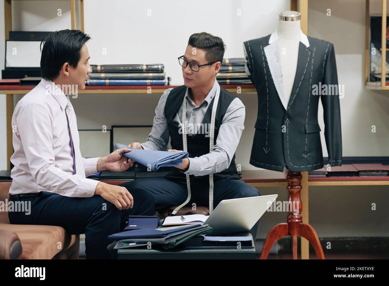 Smiling Vietnamese tailor offering various fabric to client Stock Photo ...